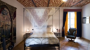 Quarto com cama, uma cadeira, uma mesa e uma janela com cortinas.