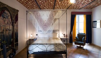 Quarto com cama, uma cadeira, uma mesa e uma janela com cortinas.