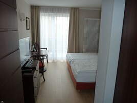 Quarto de hotel com cama, escrivaninha com computador, cadeira e janela com cortinas.