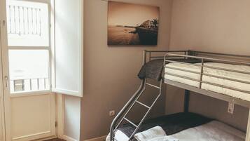 Uma cama de solteiro com escada, uma janela com vista para a praia e um quadro na parede.