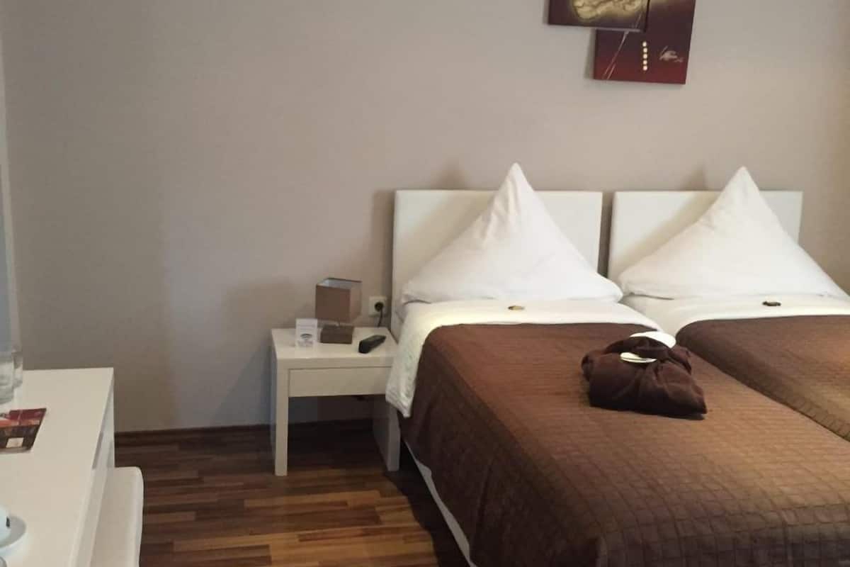 Quarto de hotel com duas camas, uma escrivaninha e uma mesa de cabeceira.
