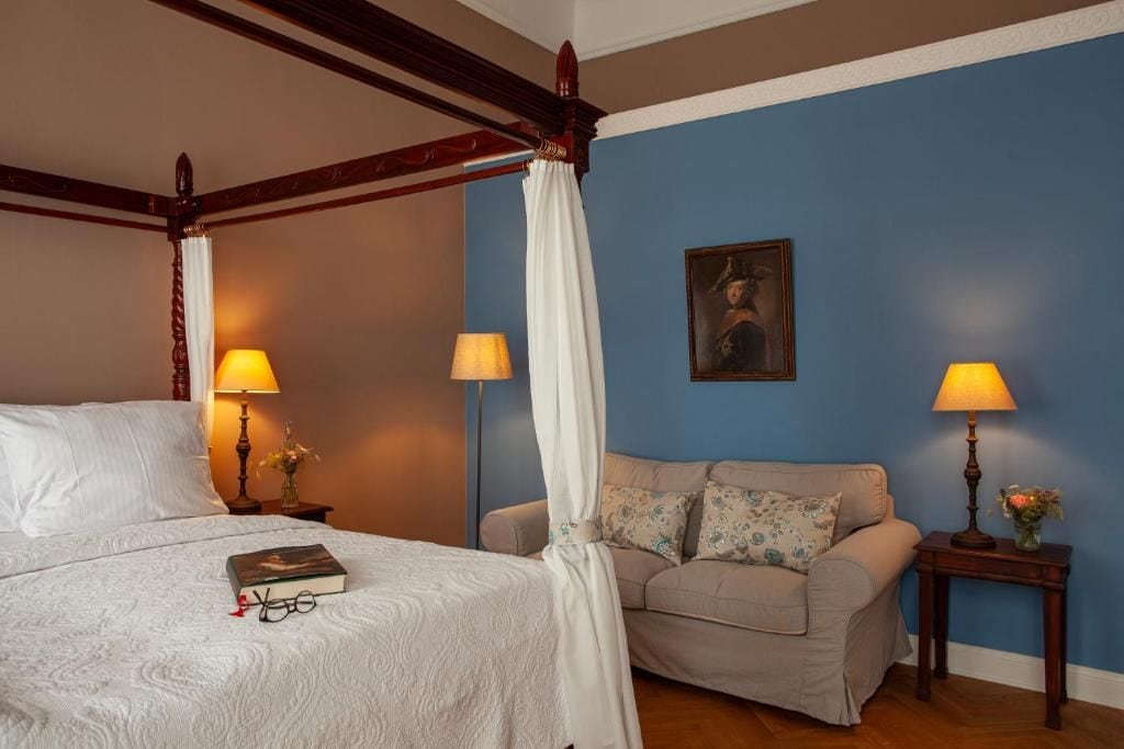 Quarto com cama de dossel, sofá, duas mesas de cabeceira com abajures e um quadro na parede.