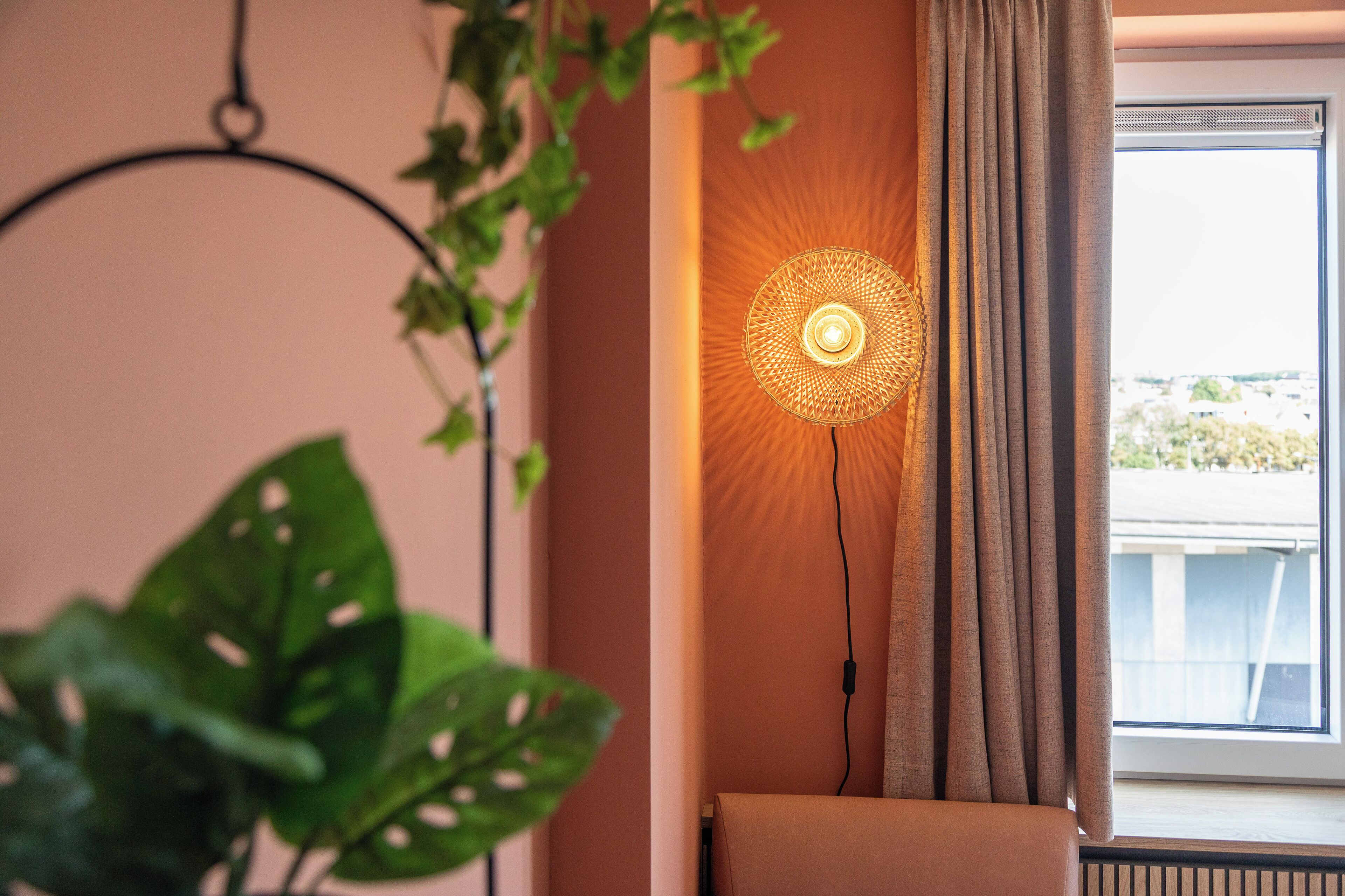 Um quarto com luminária pendente, janela com cortinas e uma planta.