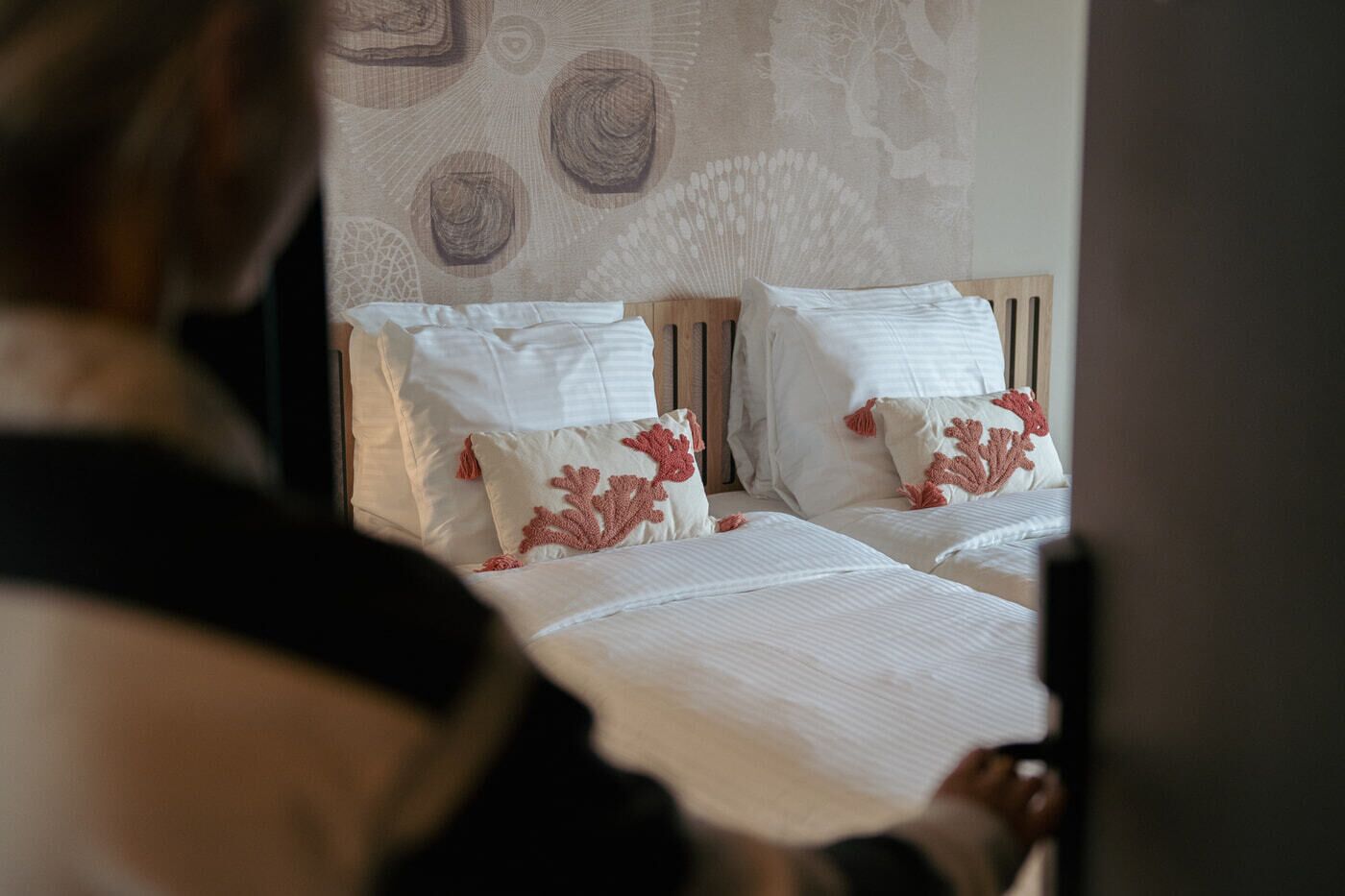 Quarto de hotel com duas camas, cada uma com roupa de cama branca e almofadas florais vermelhas.
