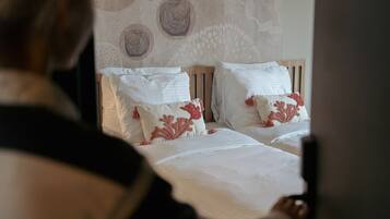 Quarto de hotel com duas camas, cada uma com roupa de cama branca e almofadas florais vermelhas.