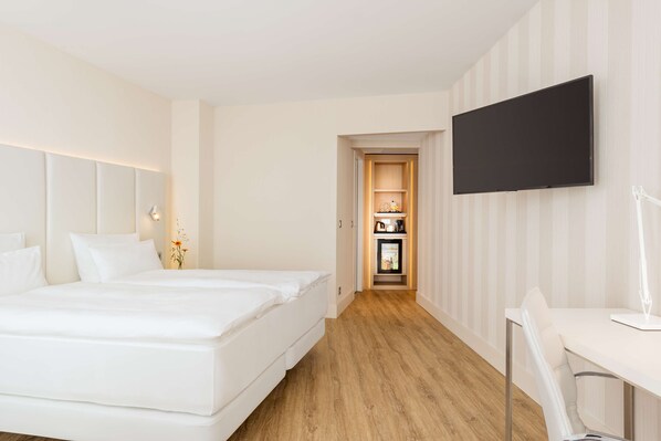 Quarto de hotel moderno com uma cama grande, uma escrivaninha e uma TV na parede.