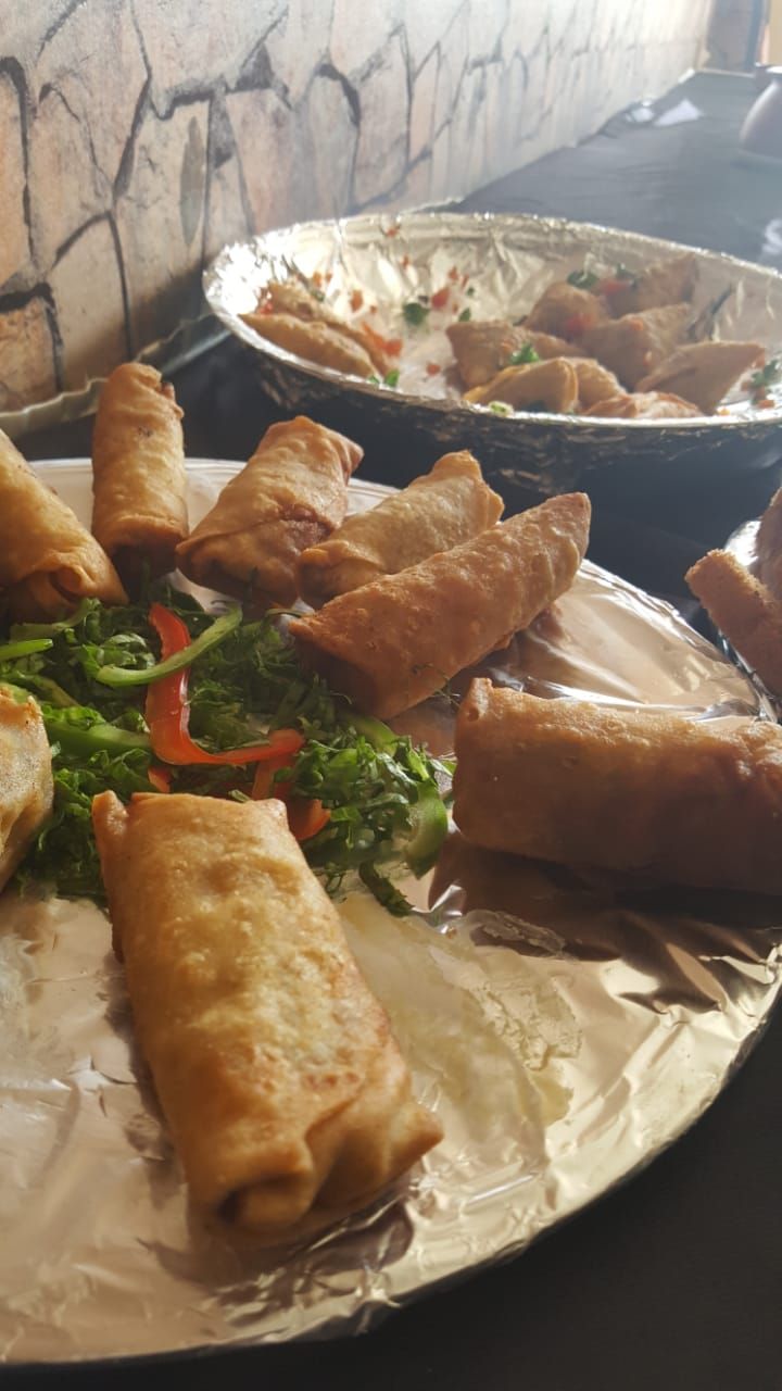 Um prato de salgados fritos acompanhado de folhas verdes e uma travessa com mais salgados.