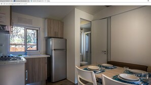 Uma cozinha compacta com geladeira, janela e área de refeições com mesa posta para dois.