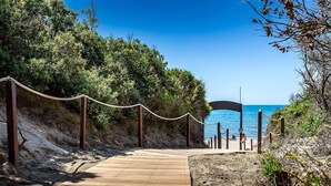 Uma passarela de madeira que leva a uma praia, com uma barreira de corda e postes de madeira.