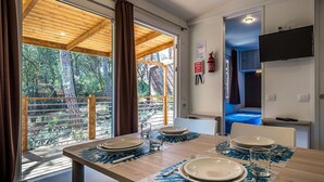 Uma sala de jantar com uma mesa posta para quatro pessoas, uma televisão fixada na parede e vista para o exterior através de grandes janelas.