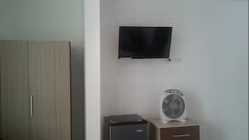 Um quarto com televisão na parede, um frigorífico pequeno e um ventilador sobre um móvel de madeira.
