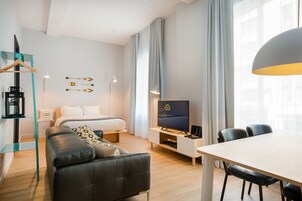 Quarto de hotel moderno com cama, sofá, mesa de jantar e televisão.