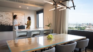 Uma área de refeições moderna com uma mesa de vidro, cadeiras cinzas e vista para a cidade.