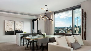 Sala de estar moderna com mesa de jantar de vidro, sofá e vista para a cidade através de grandes janelas.