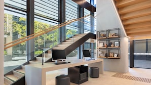 Um interior moderno com escada, uma mesa com computadores e uma estante de livros.