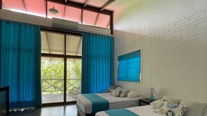 Quarto de hotel moderno com duas camas, uma janela grande com cortinas azuis, parede de tijolos brancos e teto com vigas aparentes.