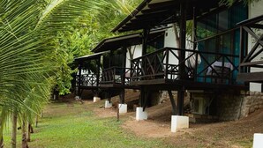 Um edifício com deck de madeira e área coberta, rodeado por vegetação e palmeiras.