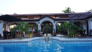 Piscina com borda em azulejo, rodeada por mobiliário de exterior e palmeiras.