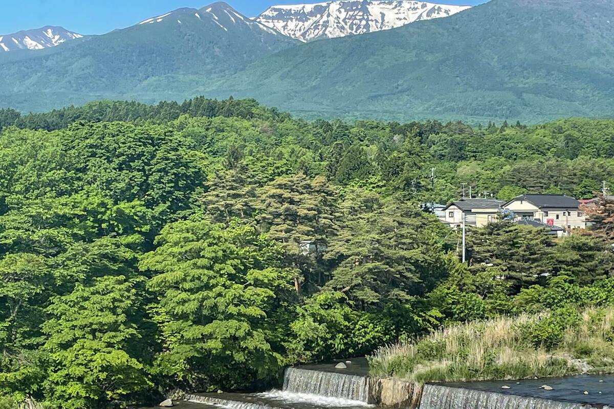 Paisagem montanhosa com floresta densa, um pequeno povoado e uma cascata.