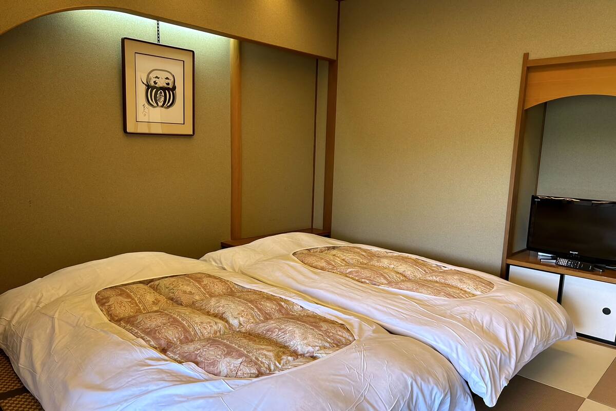 Quarto de hotel com duas camas, uma televisão sobre um suporte e um quadro na parede.
