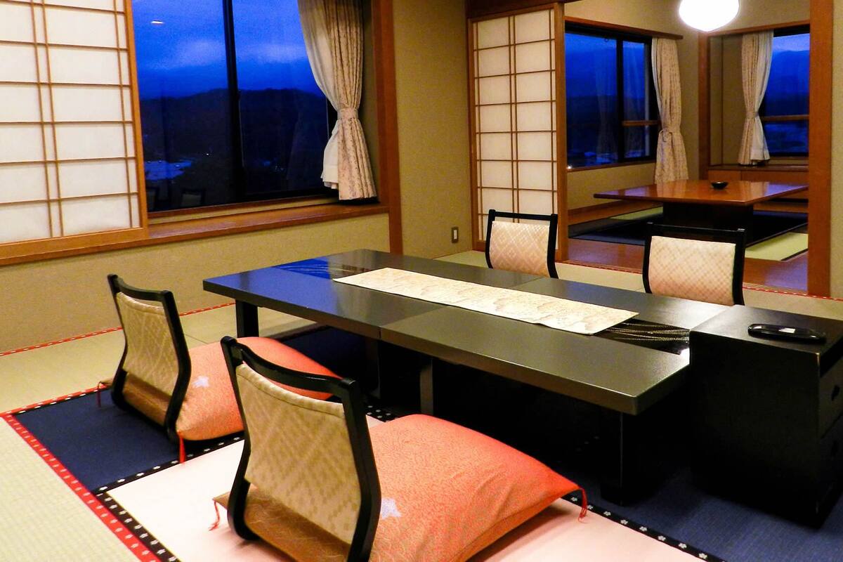 Um quarto em estilo japonês tradicional, com esteiras de tatame, uma mesa baixa e cadeiras.