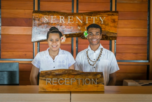 Uma mesa de recepção com uma placa de madeira que diz 'SERENITY ISLAND' e 'RECEPÇÃO'.