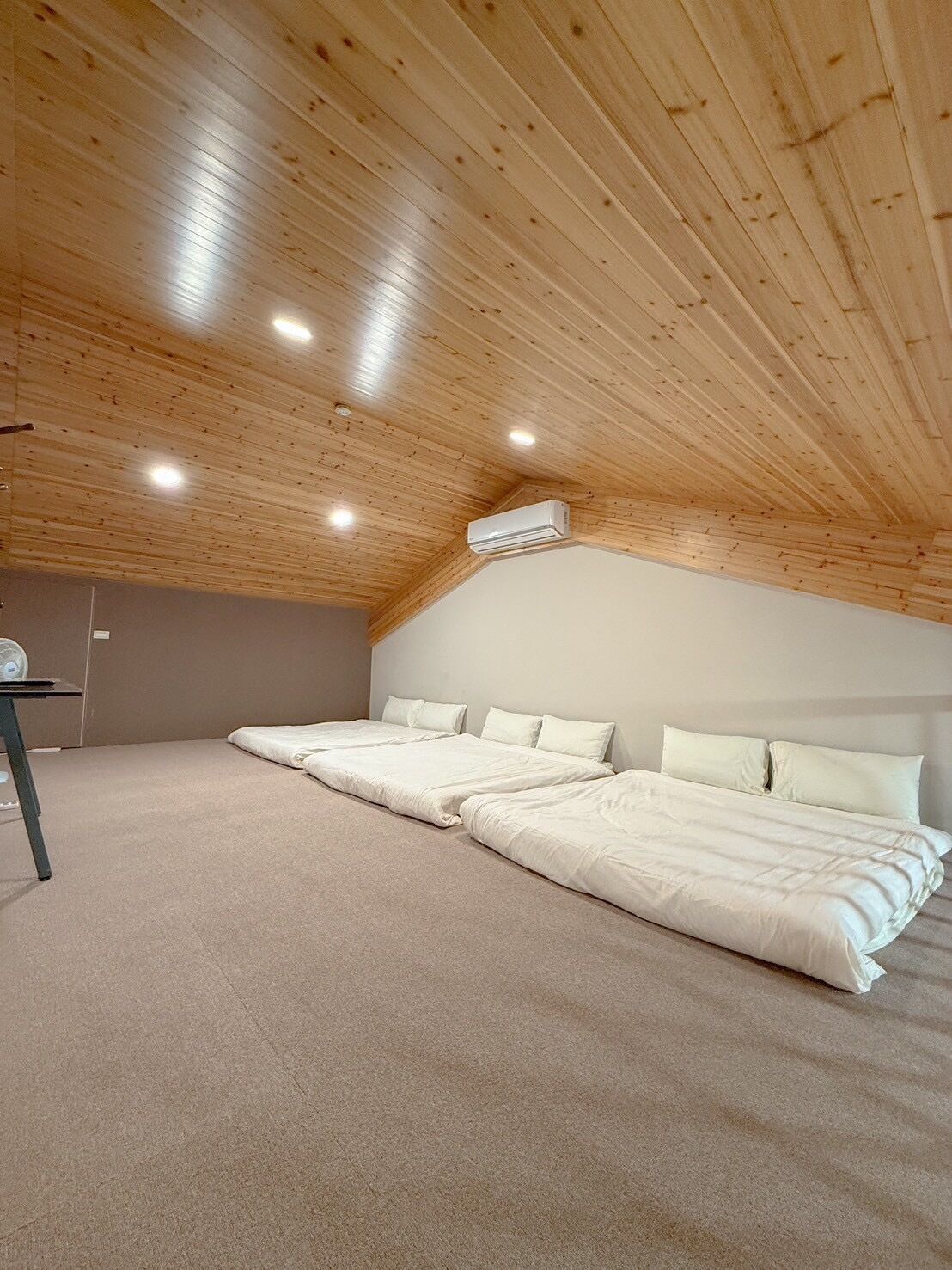 Quarto com teto inclinado, duas camas, uma escrivaninha e um aparelho de ar condicionado.