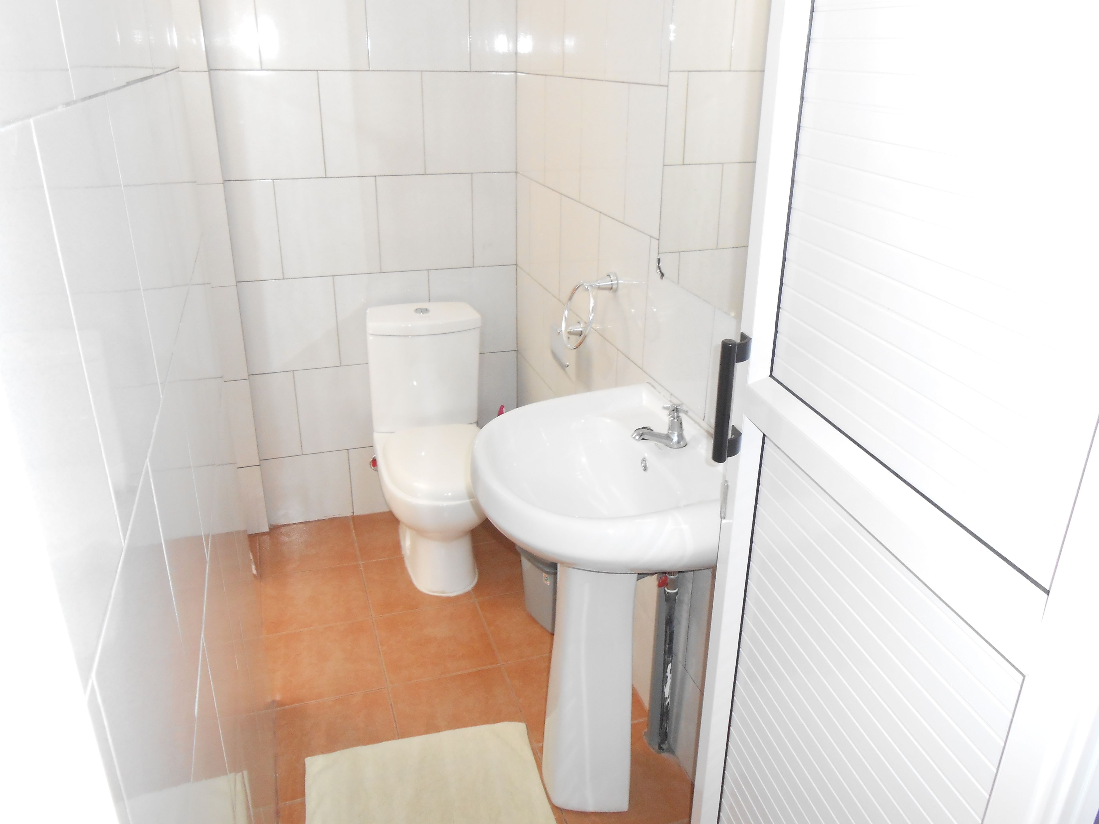 Um banheiro com azulejos brancos, vaso sanitário e pia.