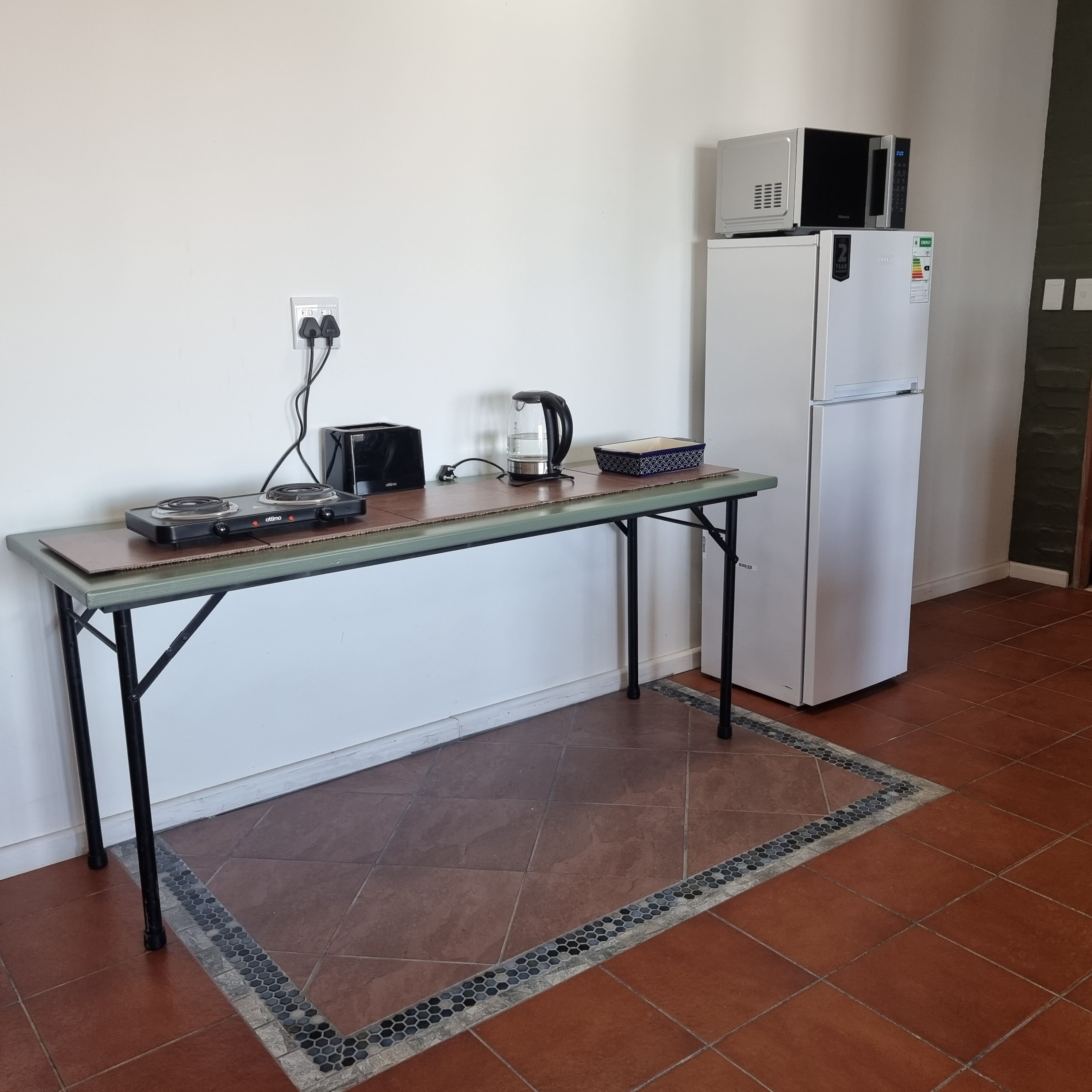 Uma pequena cozinha compacta com uma mesa, torradeira, chaleira e micro-ondas.