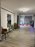 Um espaço de escritório moderno com área de recepção, duas cadeiras castanhas, luminária fixada na parede e piso de madeira.