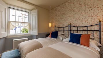 Quarto com duas camas, janela com cortinas, radiador e papel de parede floral.