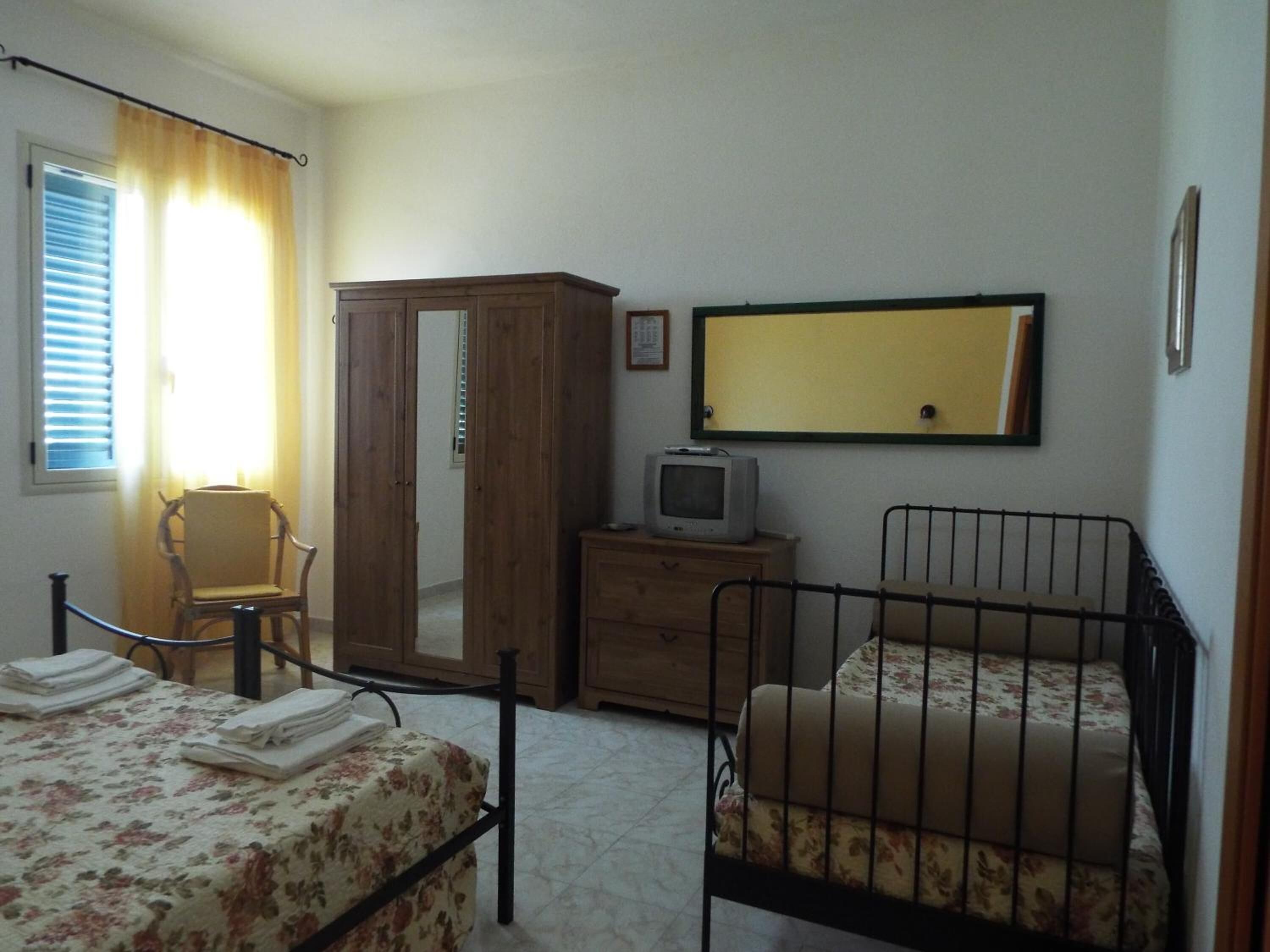 Quarto com duas camas, guarda-roupa, televisão e uma cadeira.