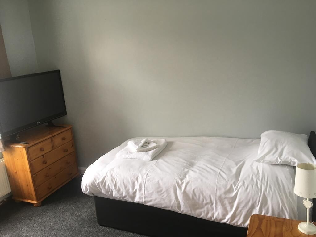Um quarto com cama, cómoda de madeira, televisão e mesa de cabeceira com abajur.