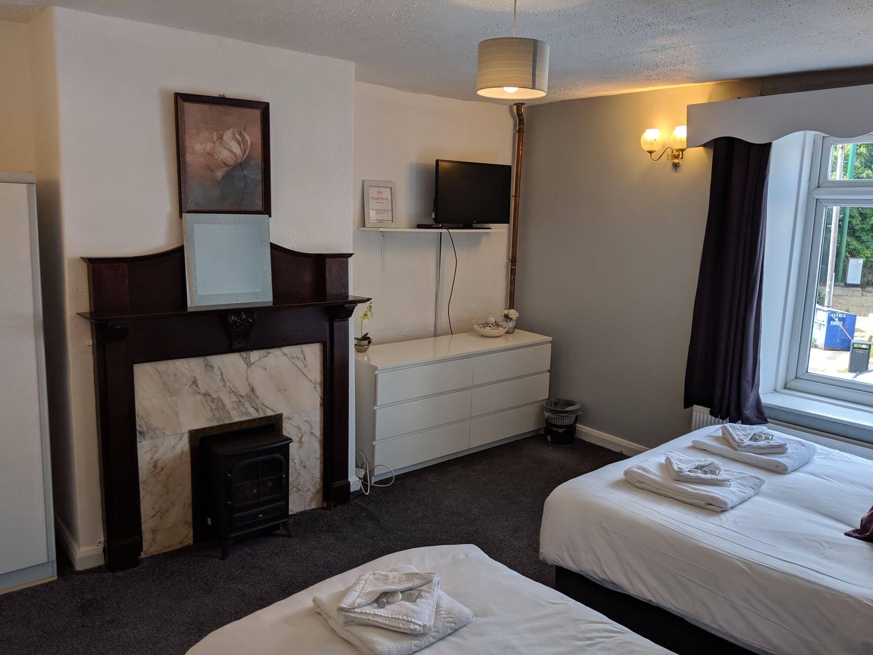 Quarto de hotel com lareira, televisão, cama com toalhas e janela com cortinas.
