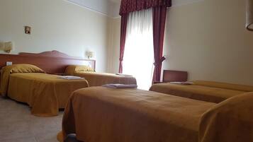 Quarto de hotel com três camas, cada uma com colcha marrom, cabeceira de madeira e mesa de cabeceira com luminária.