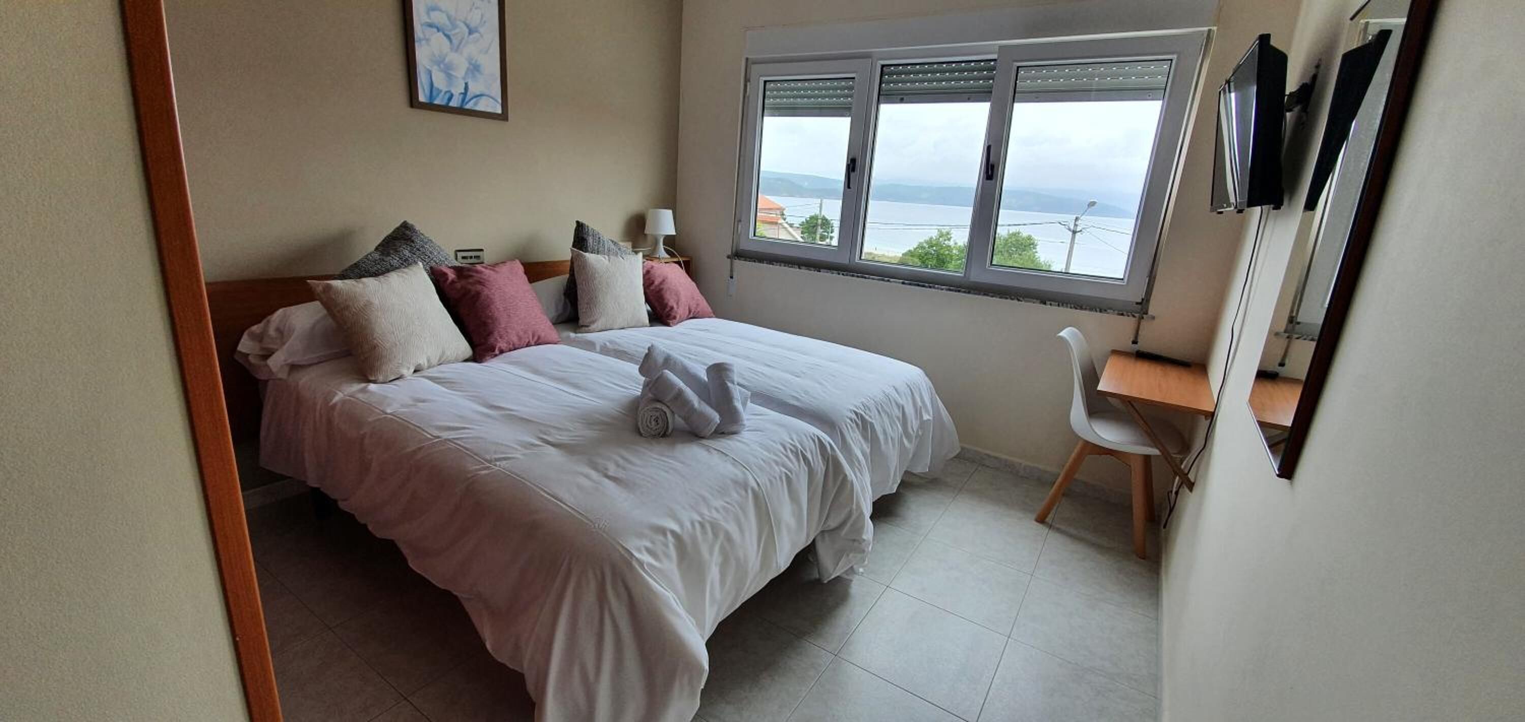 Quarto de hotel com cama, almofadas, escrivaninha e janela com vista.