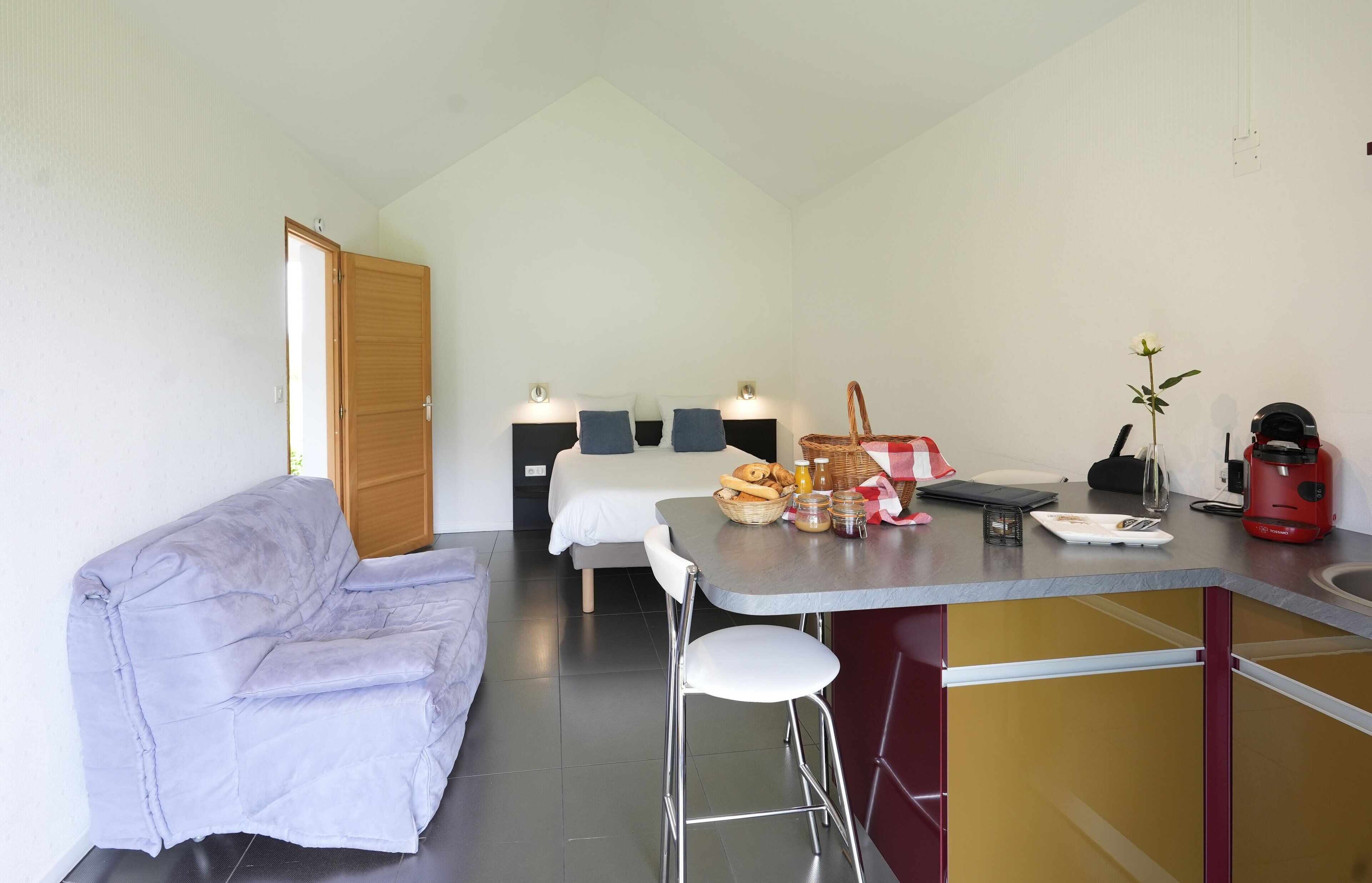 Quarto compacto com cama, pequeno espaço de cozinha, área de refeições e sofá.