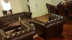 Uma sala de estar com um sofá de couro marrom escuro, uma mesa de centro de madeira e uma área de jantar com um arranjo floral.