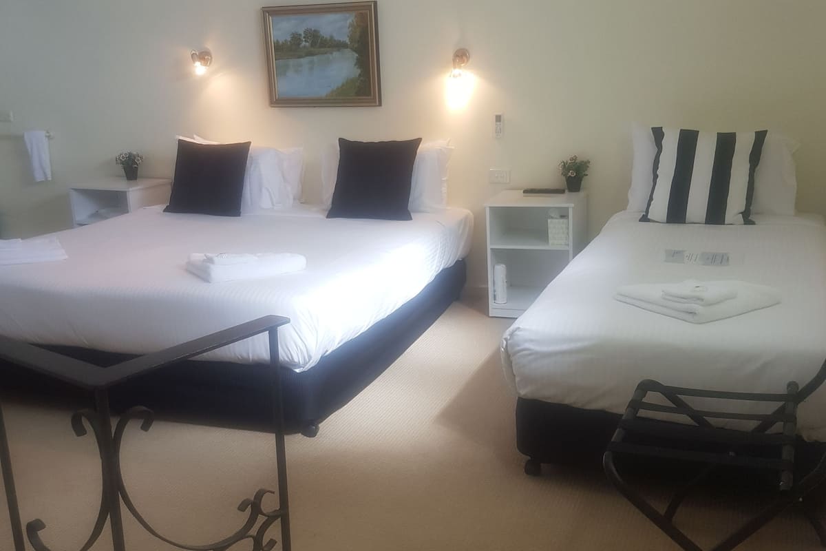 Quarto de hotel com duas camas, um quadro na parede e uma pequena mesa com uma planta.