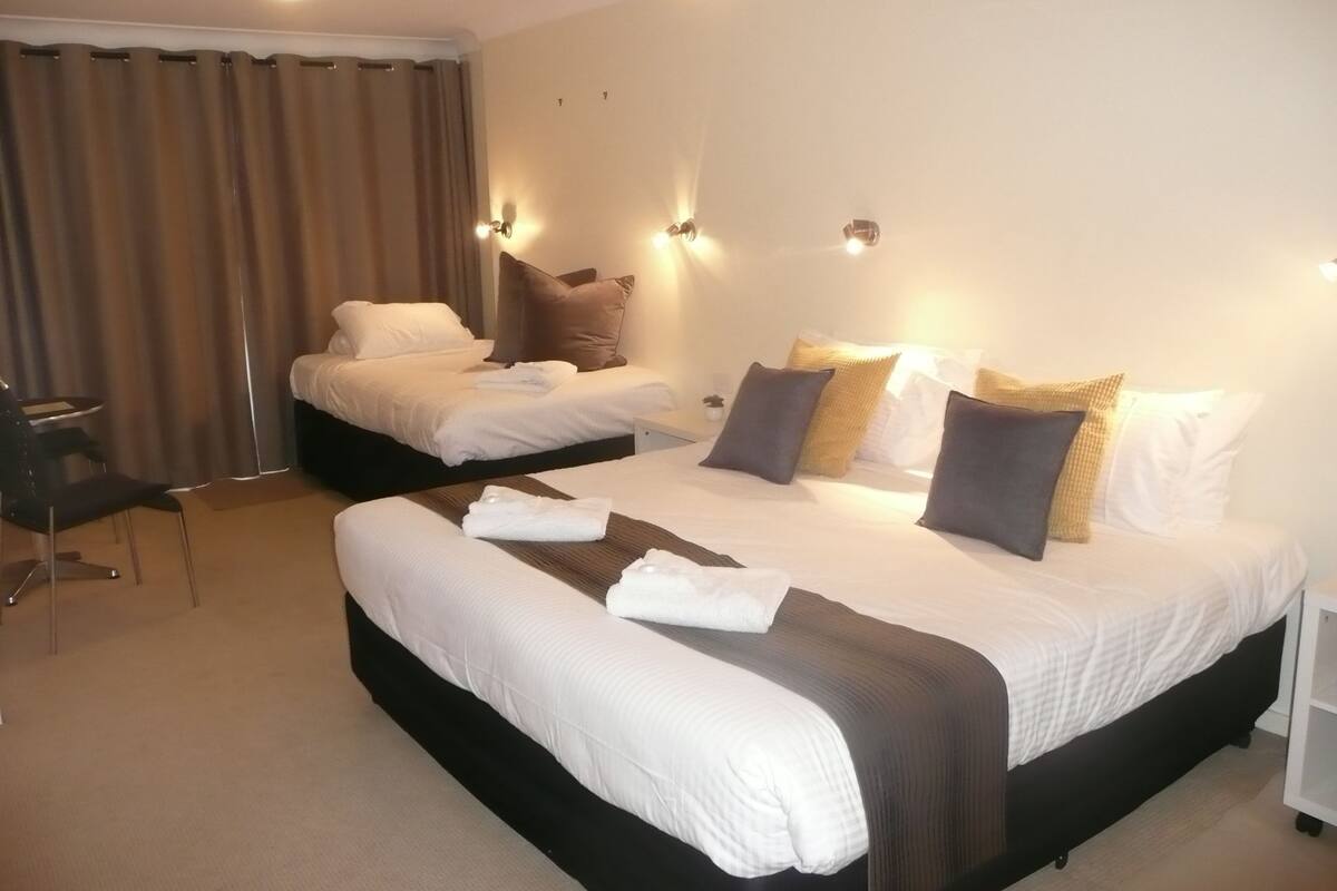 Quarto de hotel com duas camas, uma escrivaninha e uma cadeira.