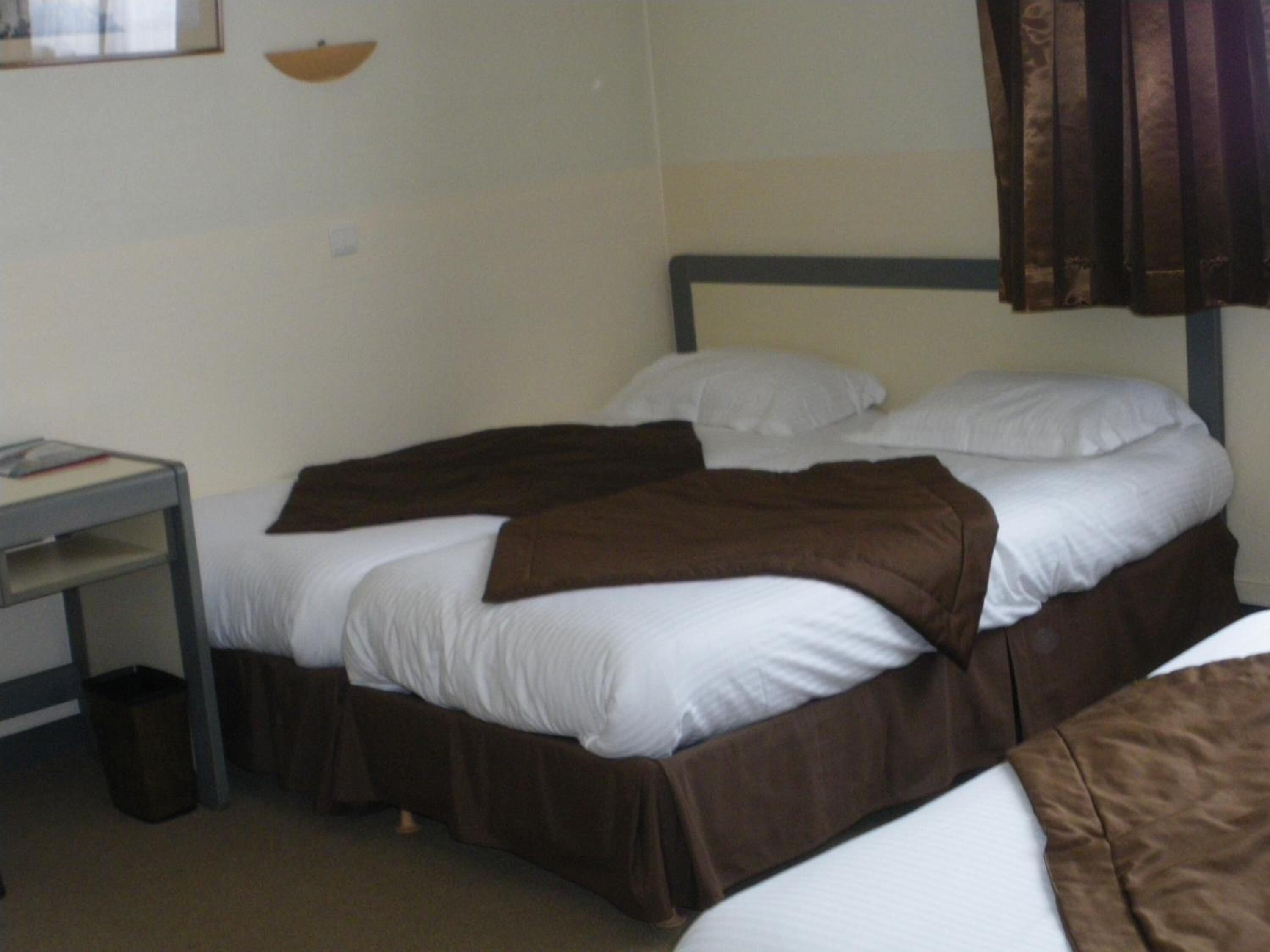 Quarto de hotel com duas camas de solteiro, uma escrivaninha pequena e um cesto de lixo.