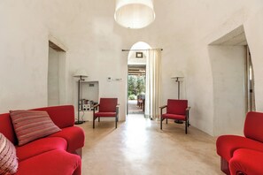Um quarto amplo com um sofá vermelho, duas poltronas vermelhas e um abajur.
