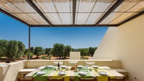Uma área de refeições com uma mesa posta para quatro pessoas, com vista para um olival.