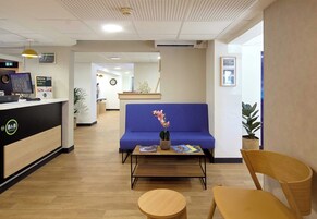 Uma área de recepção com um balcão, um sofá azul, uma mesa de centro e uma cadeira de madeira.