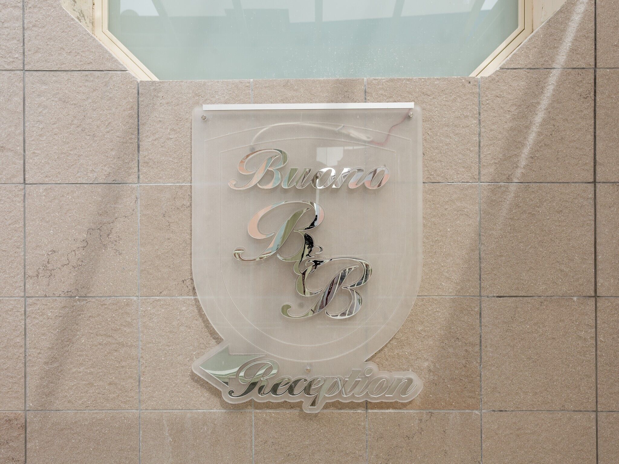 Uma placa clara e reluzente com as palavras "Bunno" e "Recepção" em uma parede revestida de azulejos.