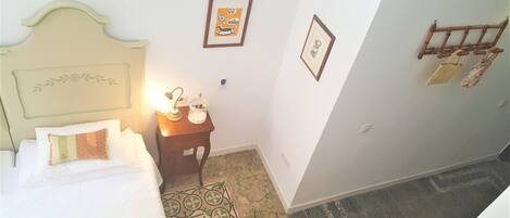 Quarto de hotel com uma cama, mesa de cabeceira com luminária, quadro emoldurado e cabideiro.