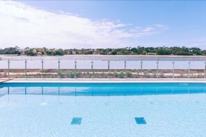 Piscina retangular com água azul cristalina, rodeada por grade de metal.