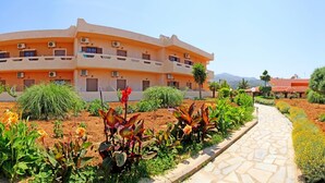 Um jardim arborizado com um caminho pavimentado, edifícios com fachadas laranja e um céu limpo.
