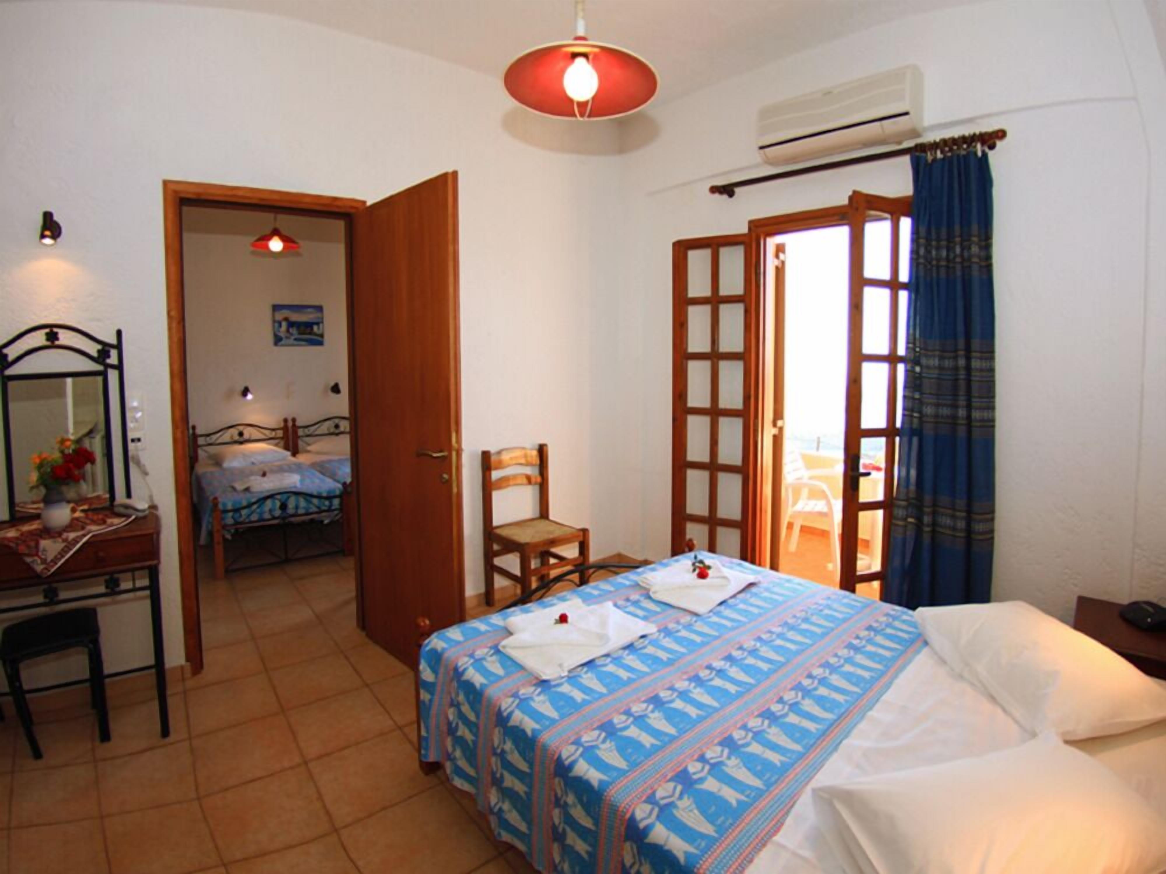 Quarto com cama, cadeira, escrivaninha e espelho. Uma porta dá acesso a outro cômodo.
