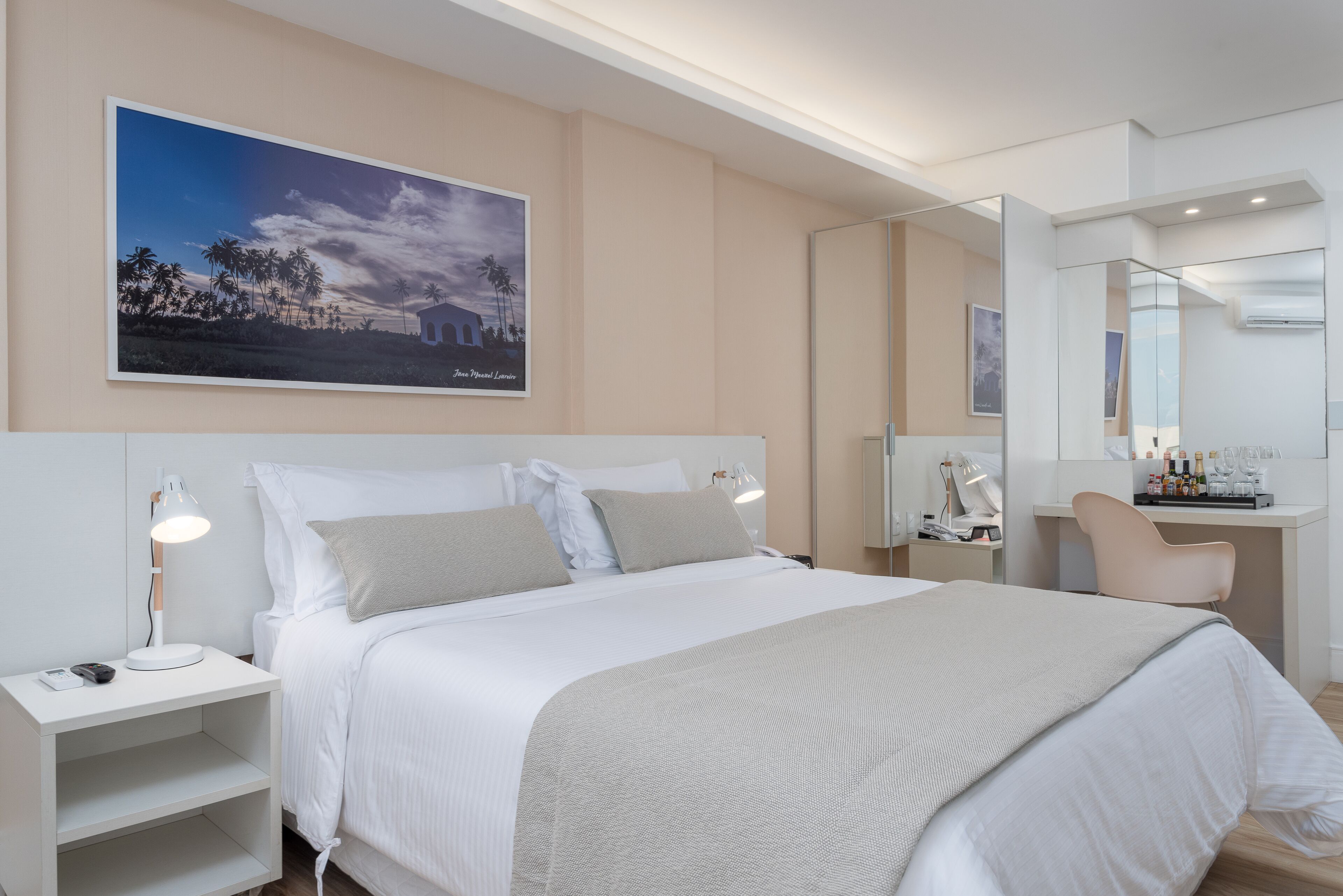 Quarto de hotel moderno com uma cama grande, mesas de cabeceira, uma escrivaninha com cadeira e uma janela ampla.